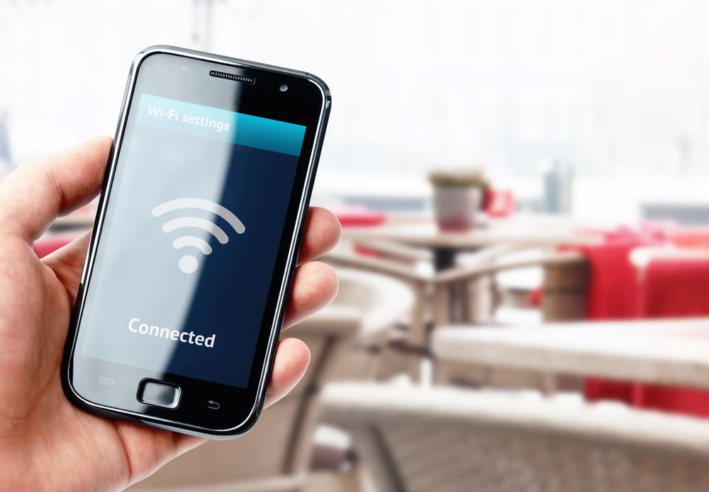 Hand holding smartphone with wi-fi connection in cafe - Custom Wirth, LLC